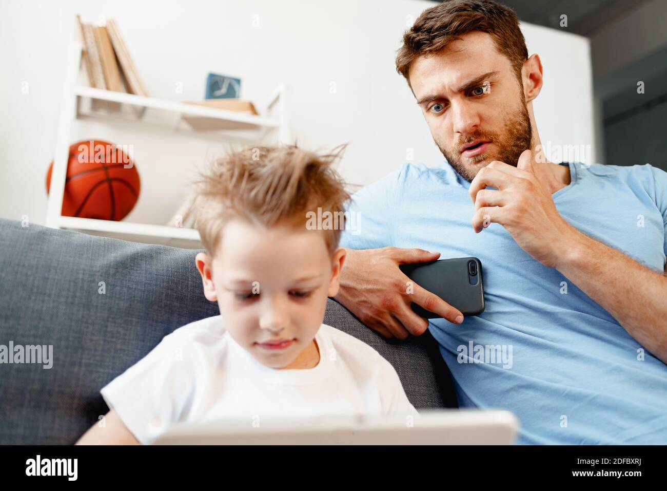 Worried father peeking at what his son is watching on digital tablet ...