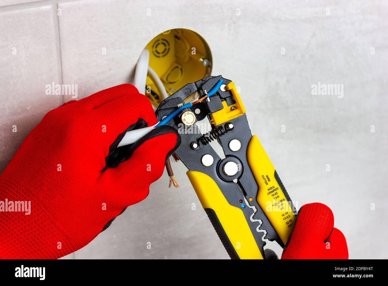 An electrician in red gloves, using wire cutters, remove insulation ...