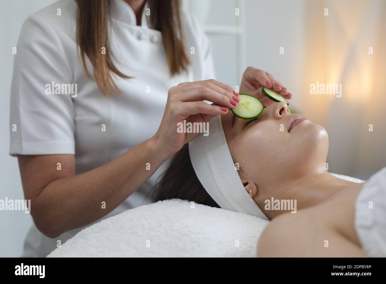 Caucasian Woman Lying Back While Beautician Puts Cucumbers On Her Face
