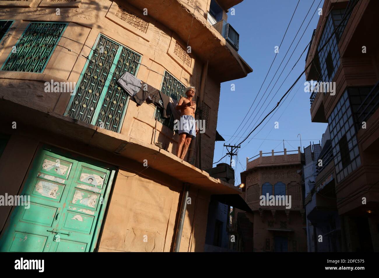 India, a man prays (early morning puja ritual) alone on the balcony of ...