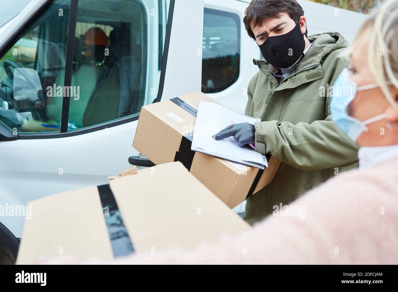 Delivery service parcel carrier with face mask asks customer to sign ...