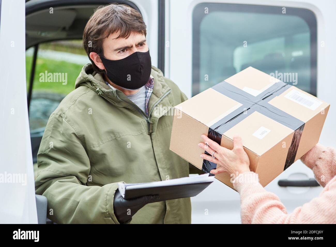 Delivery service parcel delivery man with face mask hands over package ...