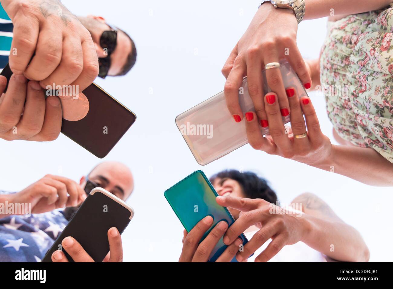 group of young friends chatting with their mobiles while smiling ...