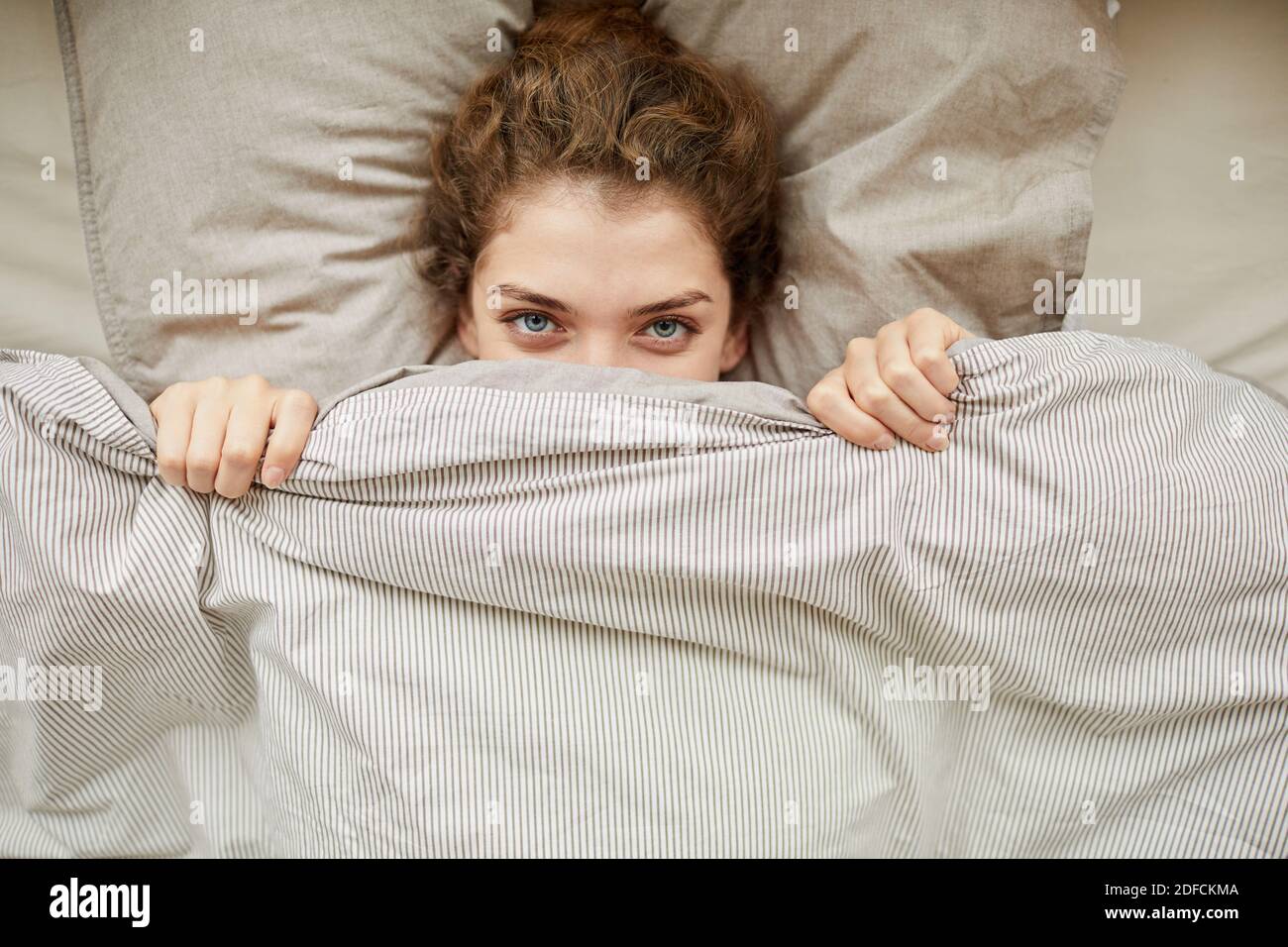 High angle view of young woman looking at camera hiding under the ...
