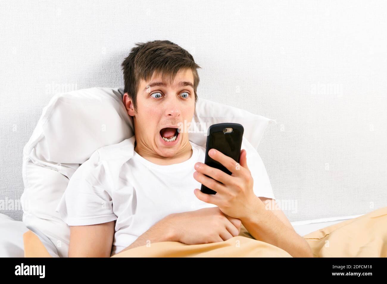 Shocked Young Man with a Phone in the Bed at the Home Stock Photo - Alamy