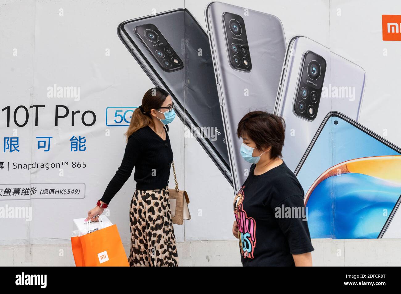 Commuters wearing face masks walk past the Xiaomi Mi 10T Pro 5G ...