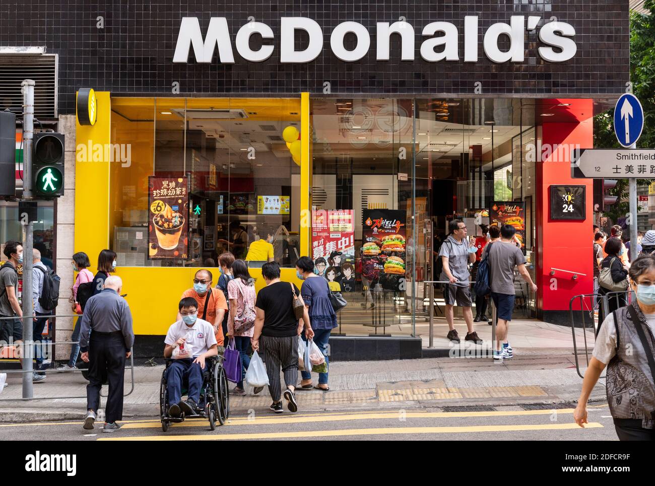 Pedestrians wearing face masks cross the street at a traffic light in ...