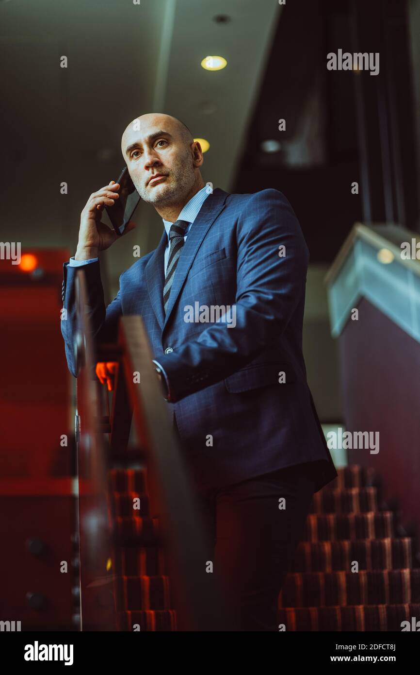 Middle aged bald businessman stopped on the stairs holding smartphone ...