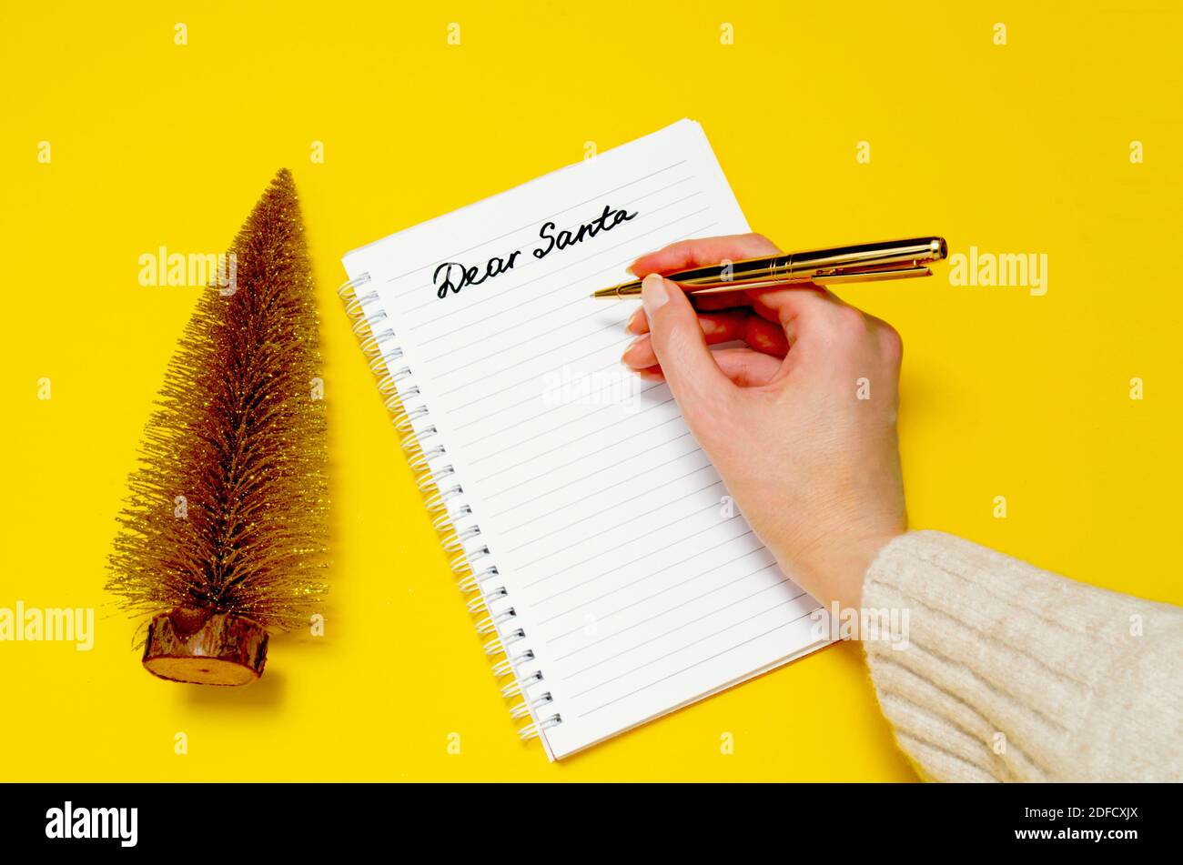 Female hand writing letter to Santa on yellow background. Golden ...