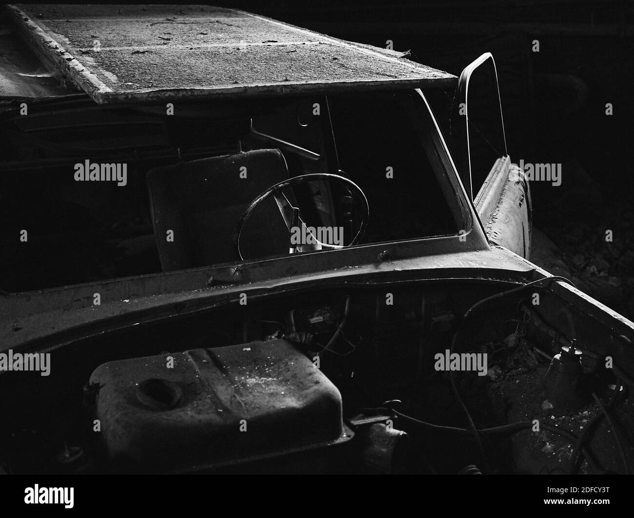 A greyscale closeup of an old car with dismantled parts in an old ...