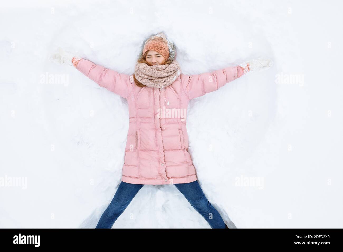happy woman lying in the snow and moving arms and legs up and down ...