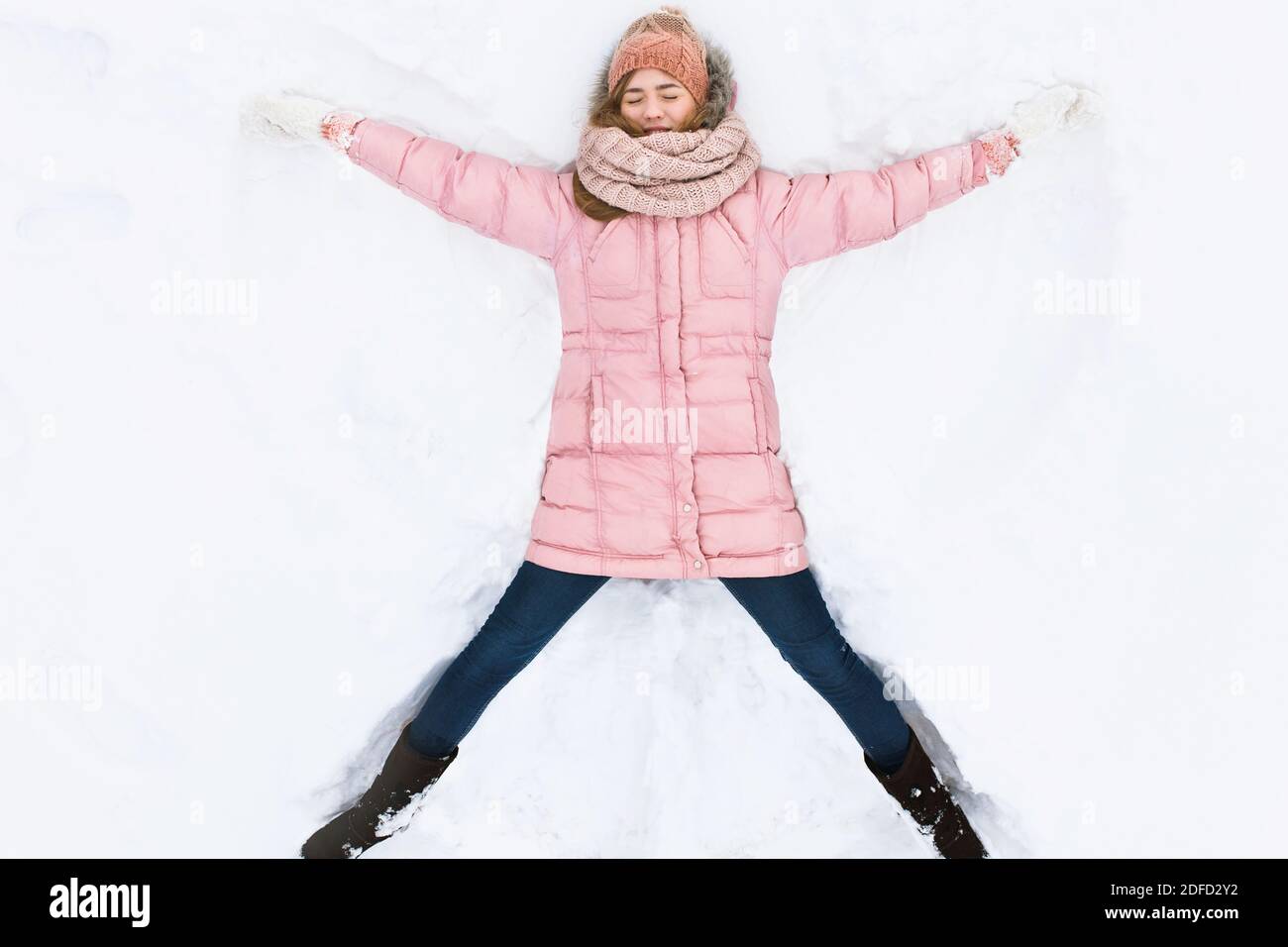 happy woman lying in the snow and moving arms and legs up and down ...