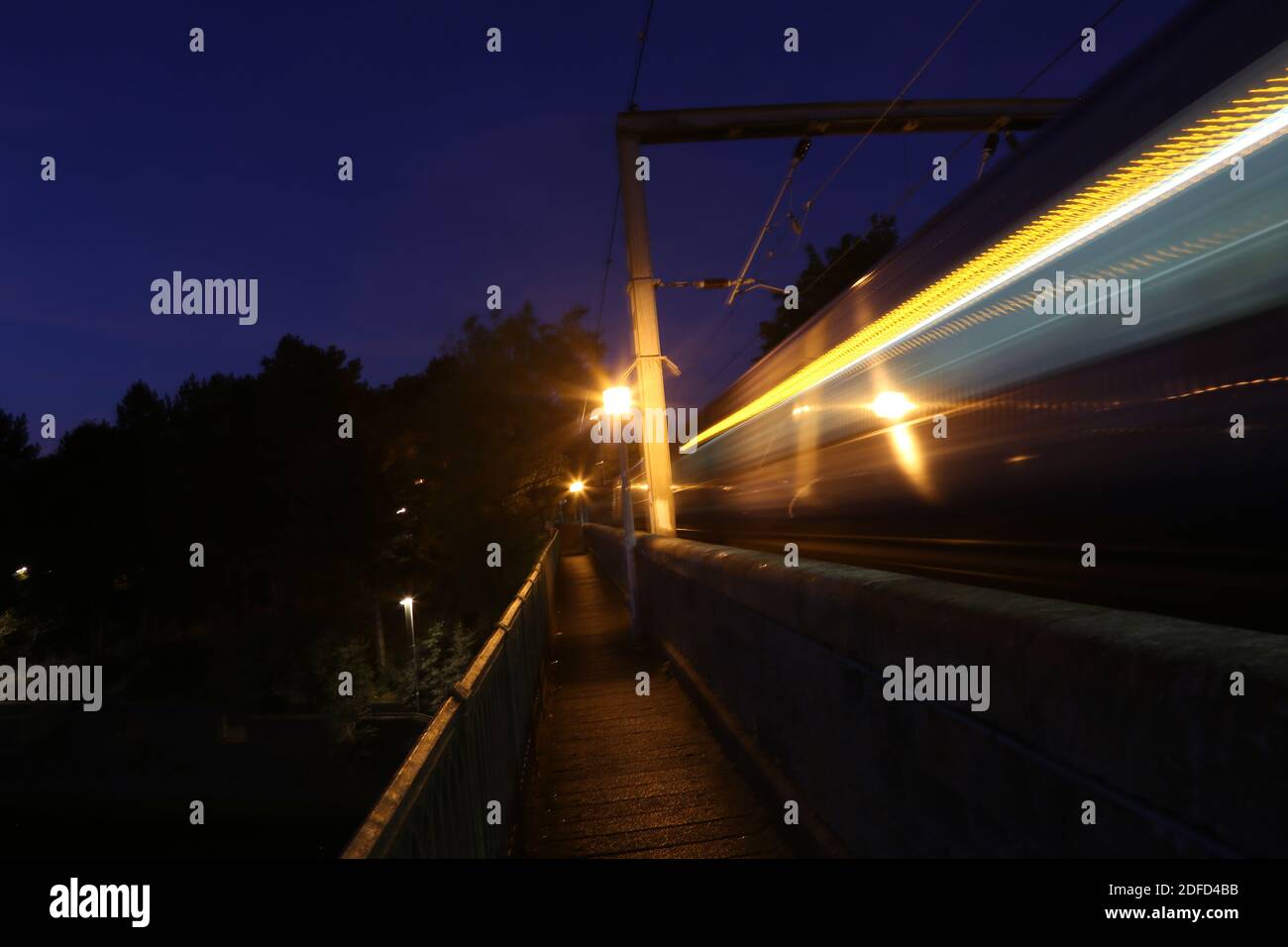 Train moving across rail bridge at night leaving light trail Stock ...