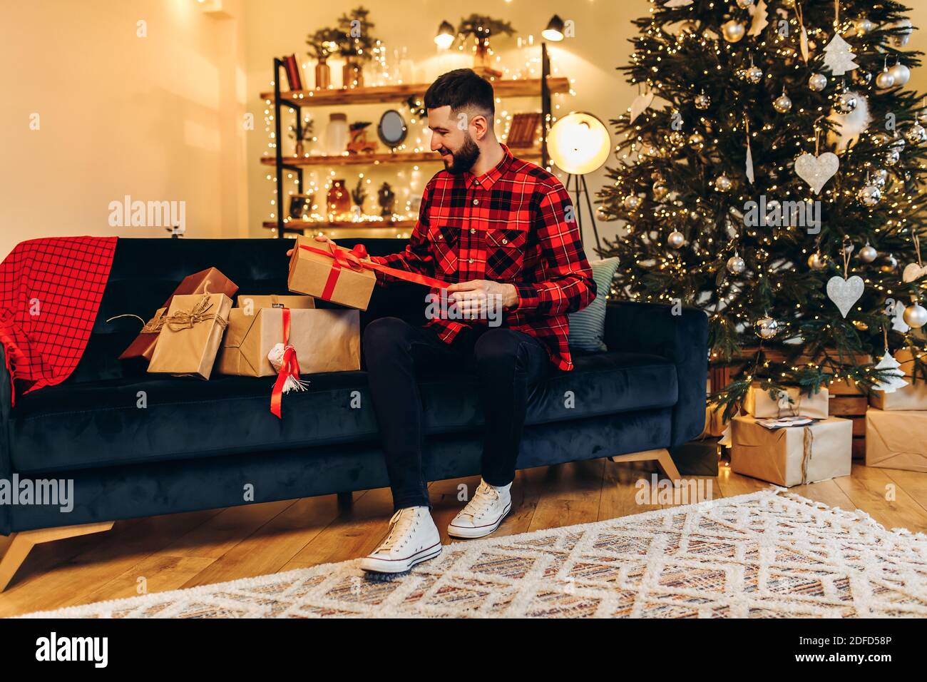Happy young man opening Christmas gifts at home against the background ...