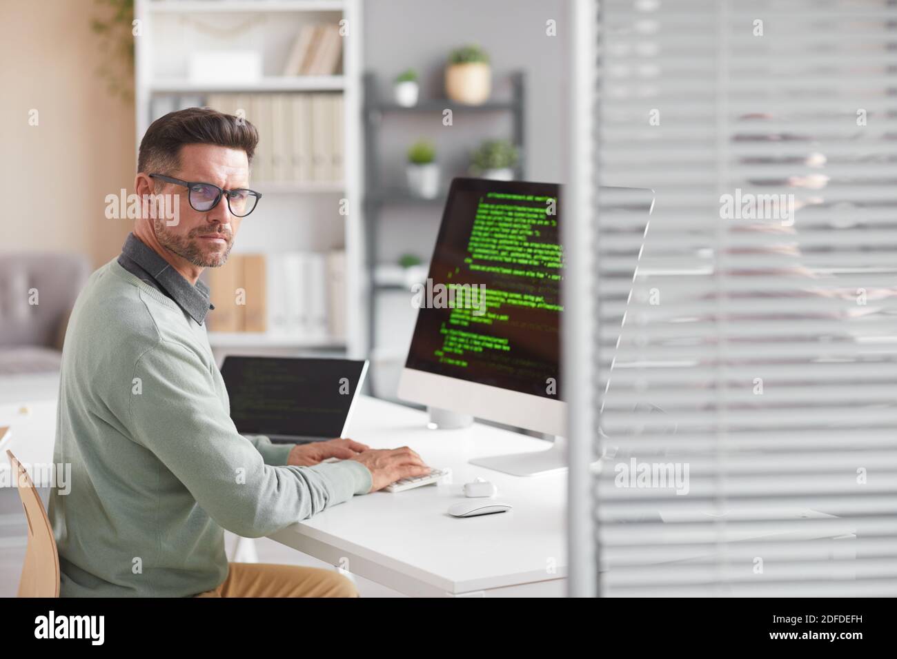 Portrait of mature developer looking at camera while working at the table with computer in ...