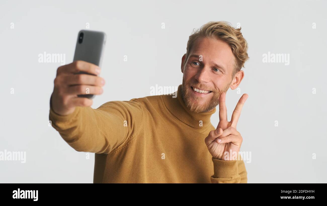 Attractive stylish bearded man showing peace gesture making selfie ...