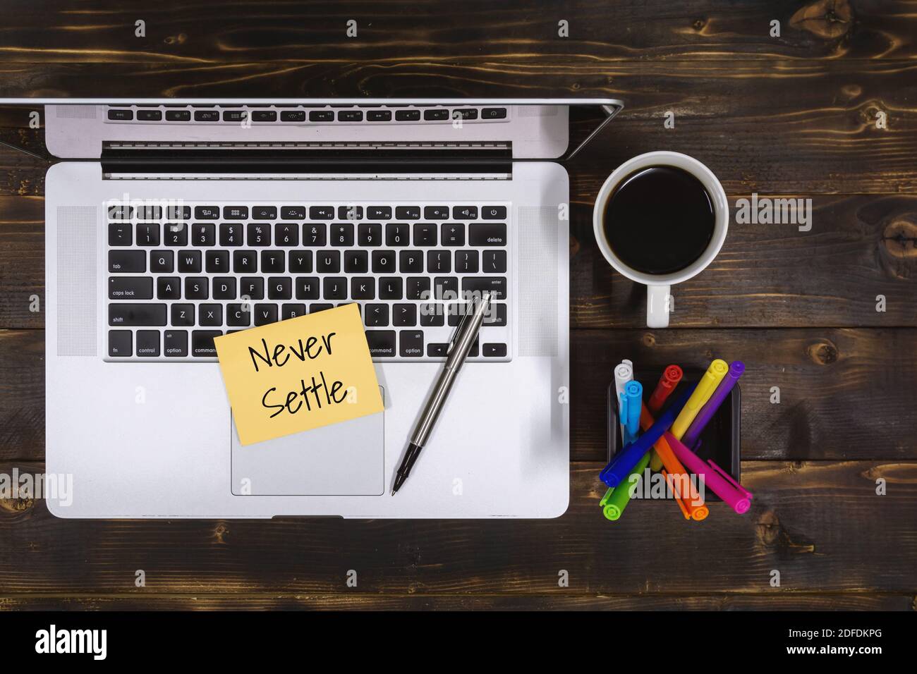 Never Settle. Overhead view of Sticky Note and Laptop on Rustic Wood ...
