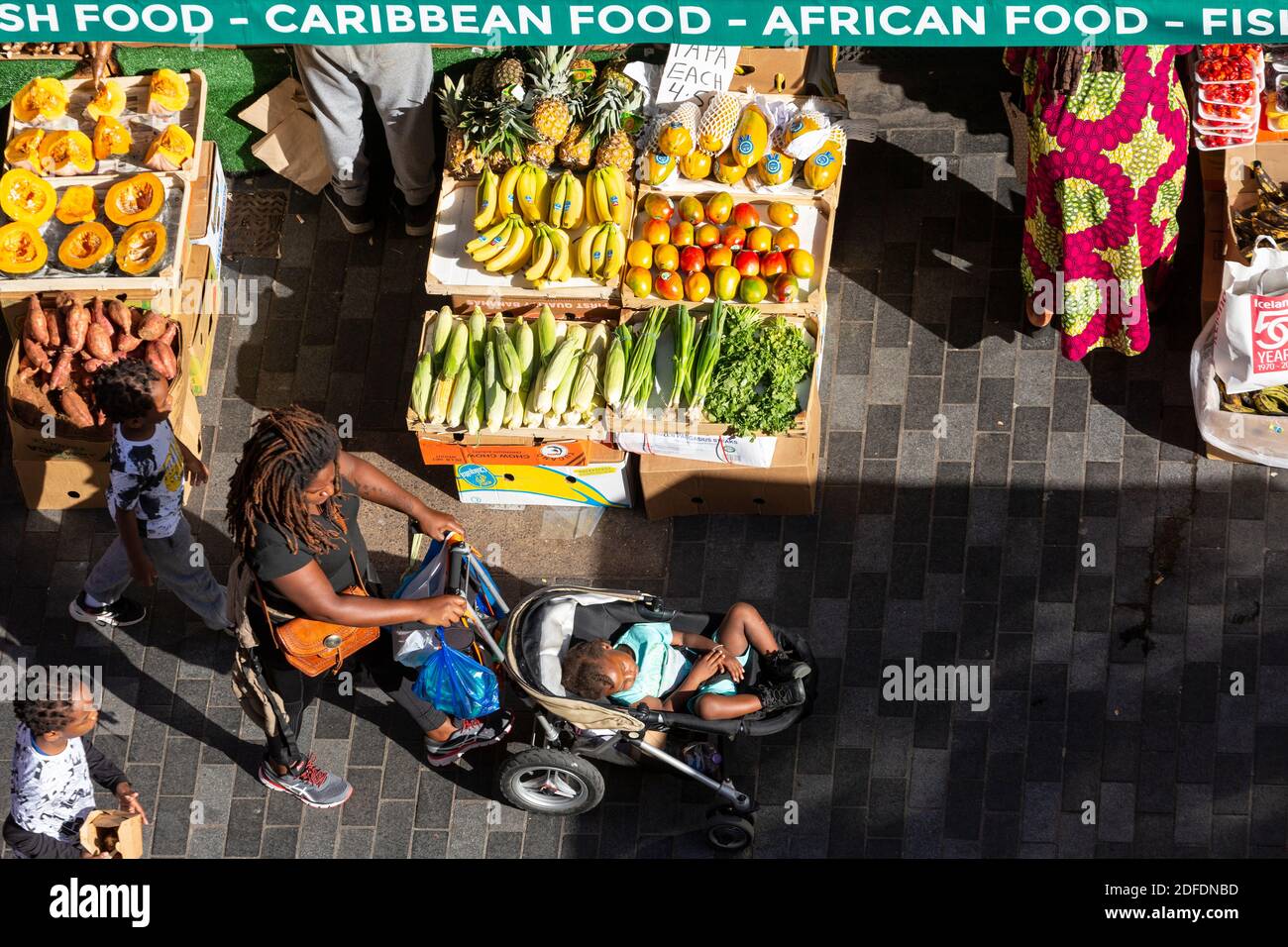 A woman with pushchair passing a street stall at Brixton Market ...