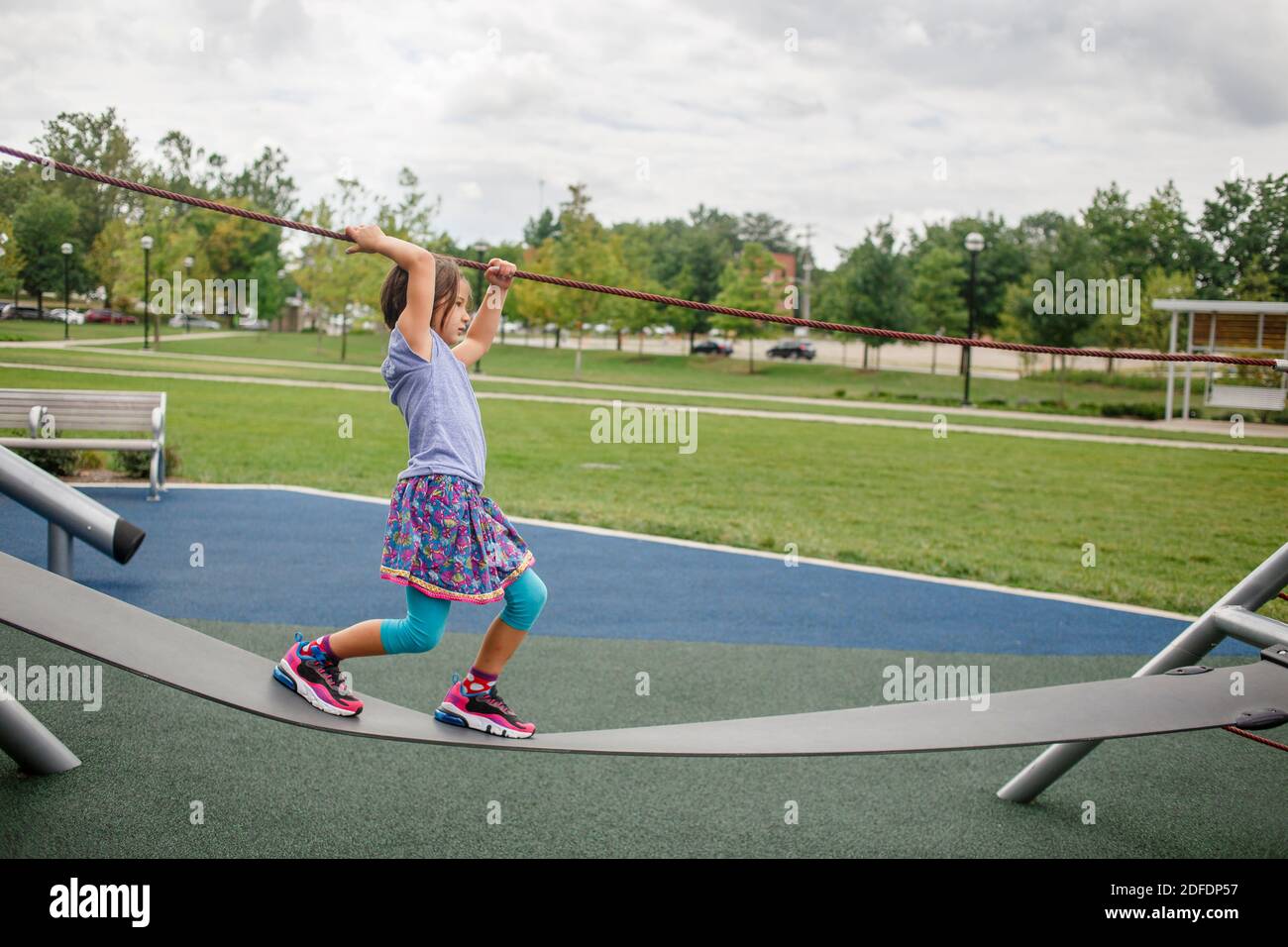 A little girl balances on playground equipment outside in summertime ...