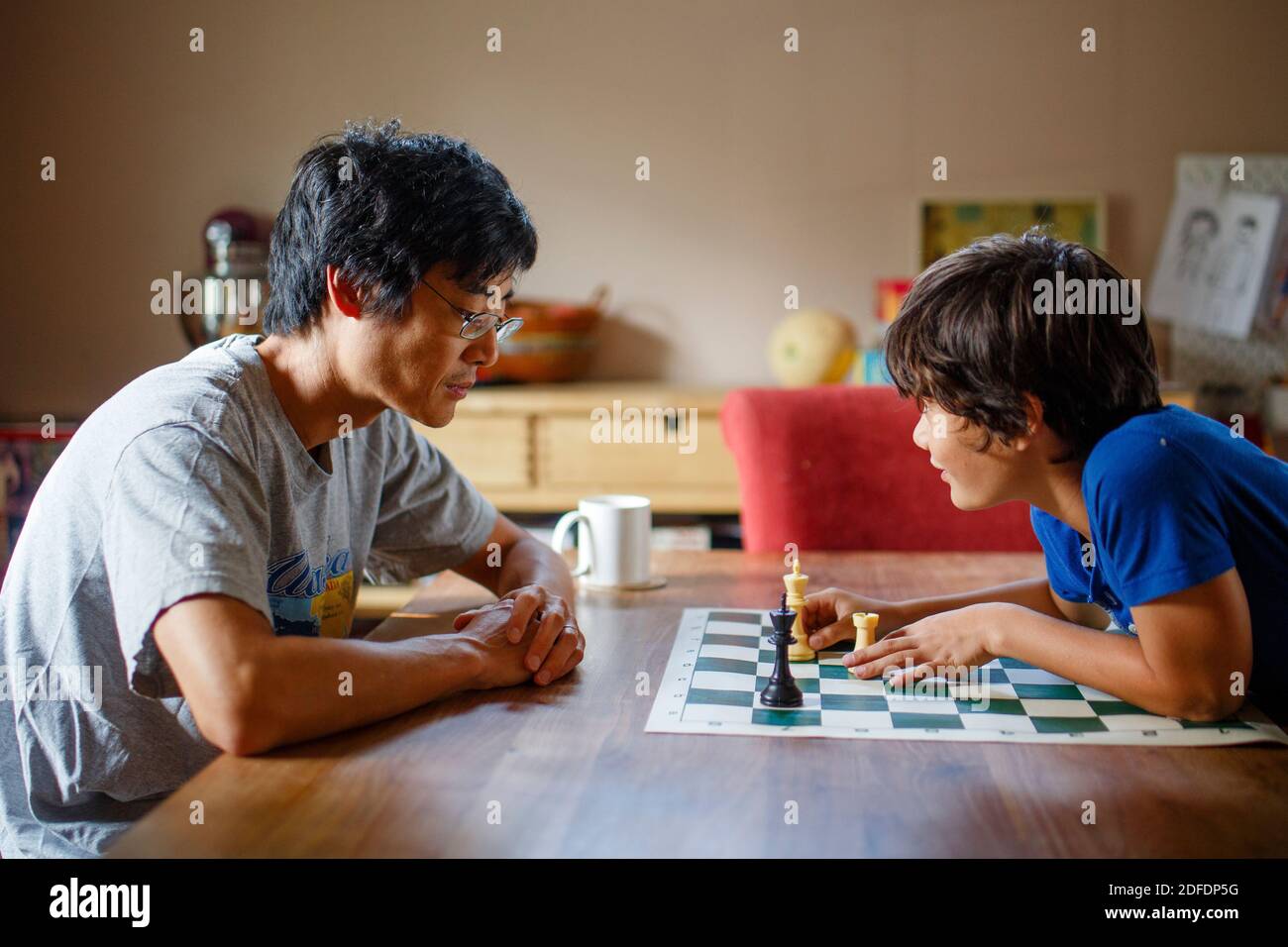 A boy makes chess move while playing with father at dining room table ...