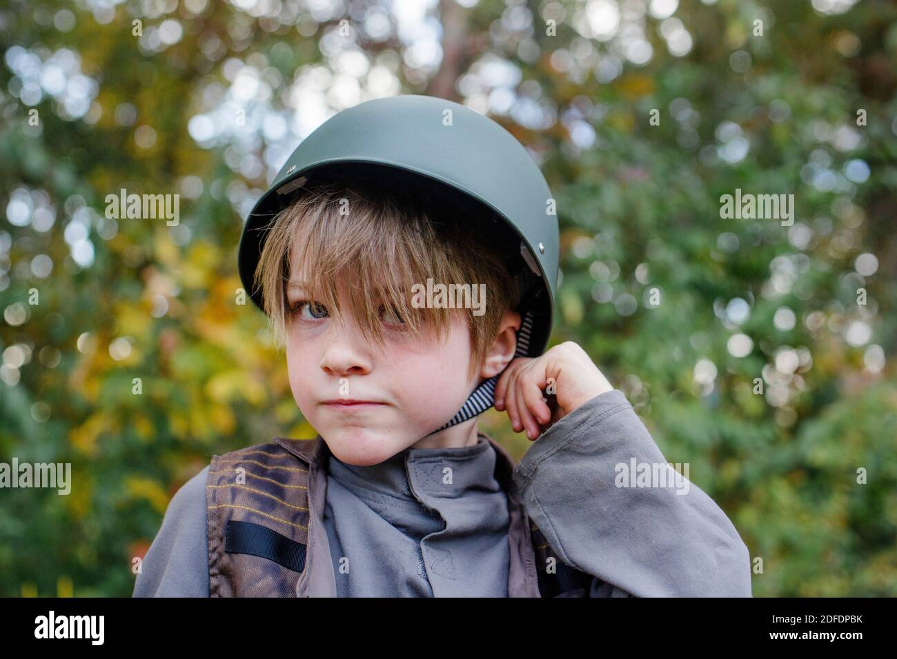 A boy dressed in a soldier costume tugs at the strap of his helmet ...