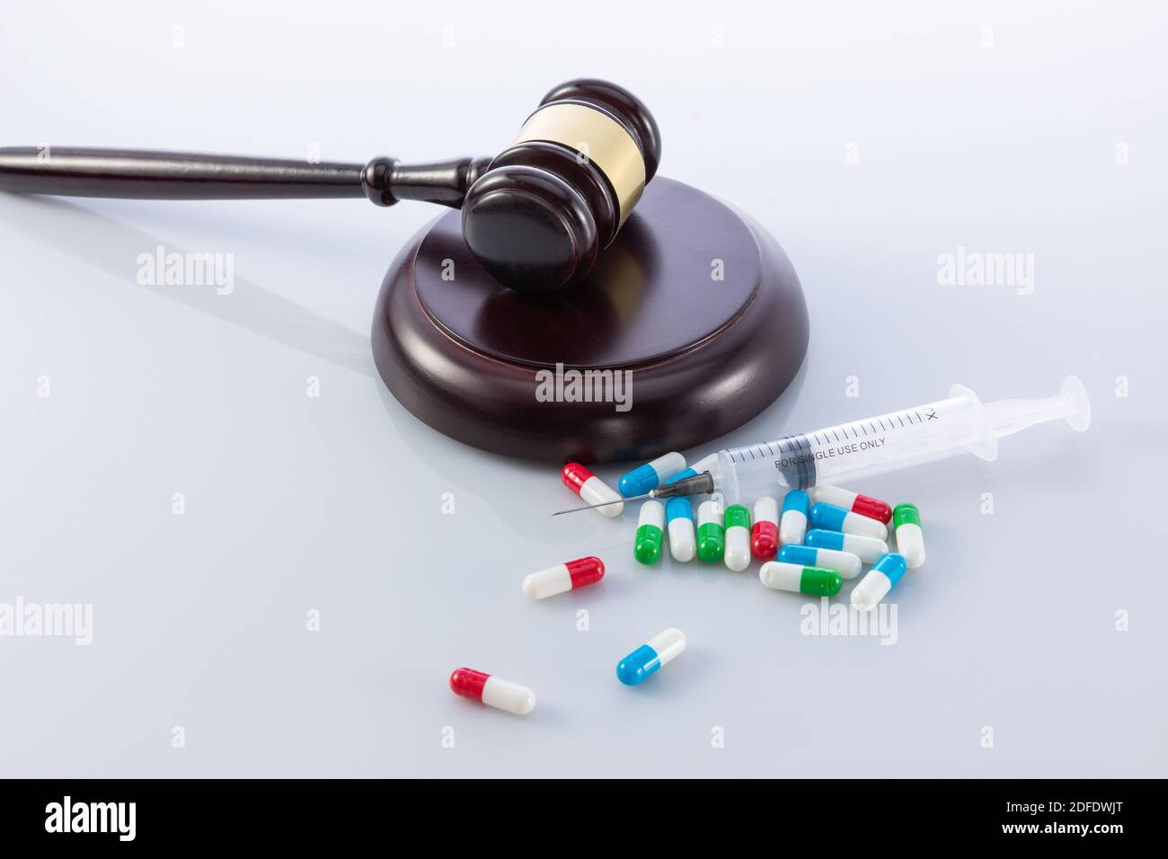 A high angle shot a gavel with pills and a syringe on a white ...