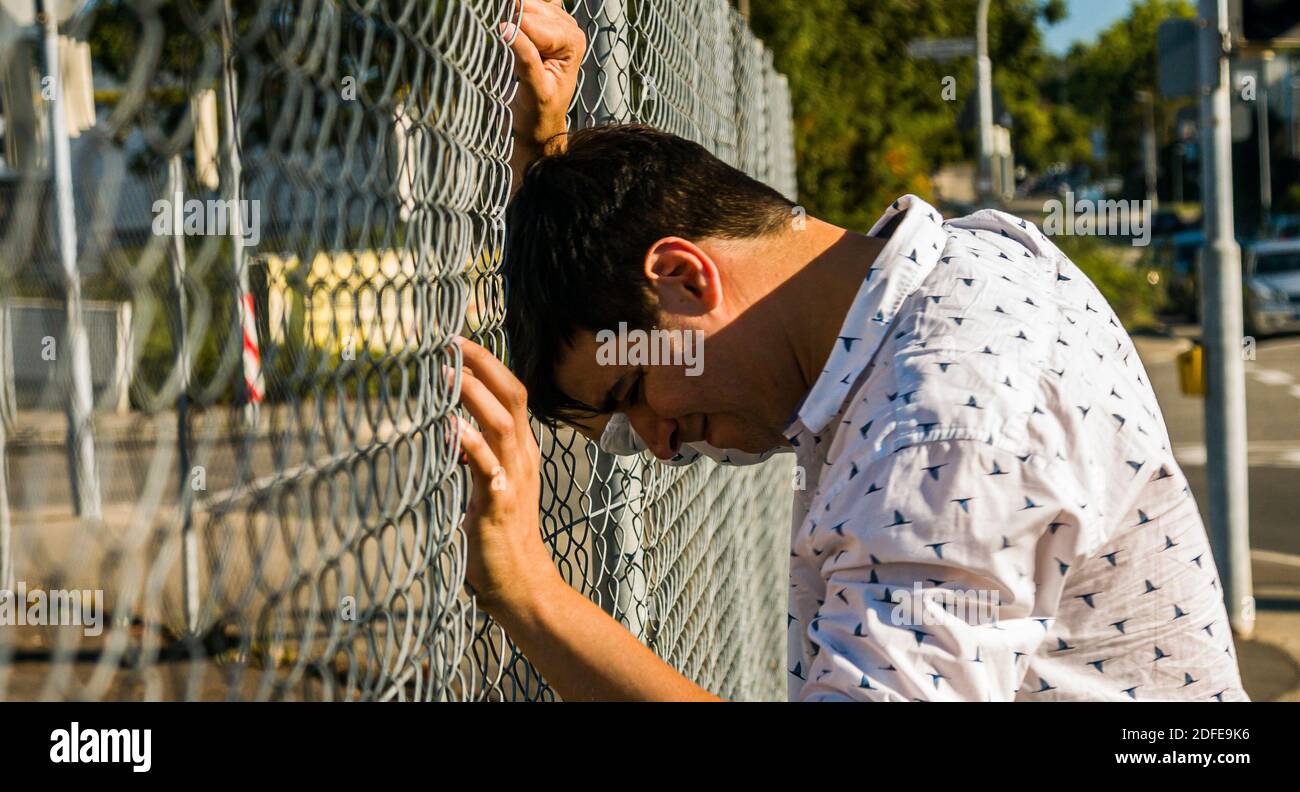 Distraught man crying and pushing head against fence. Profile view ...