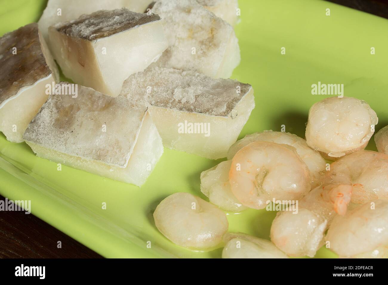 Green platter with thawed cod fillets and prawns. Raw ingredients for ...