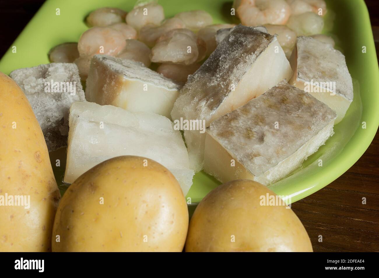 Some raw cod fillets with whole potatoes and prawns in the background ...
