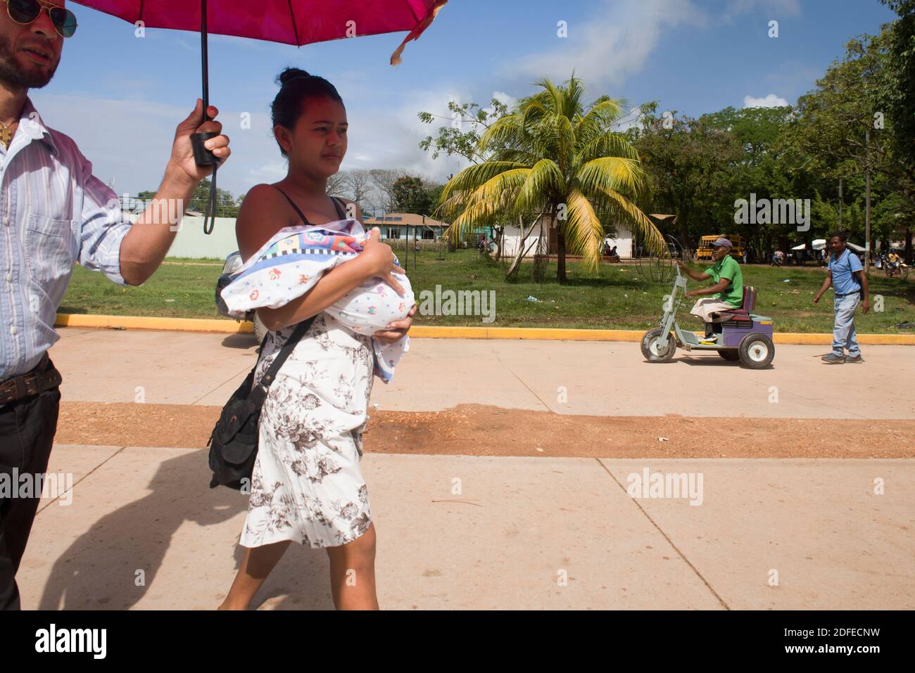 Young woman carrying her baby with husband holding a sun umbrella to ...