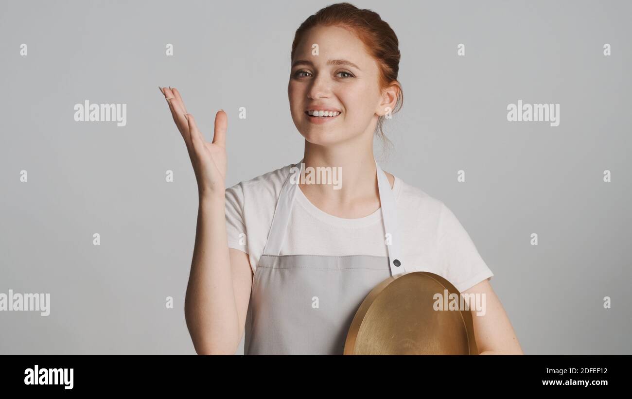 Attractive waitress in apron with tray joyfully posing on camera over ...