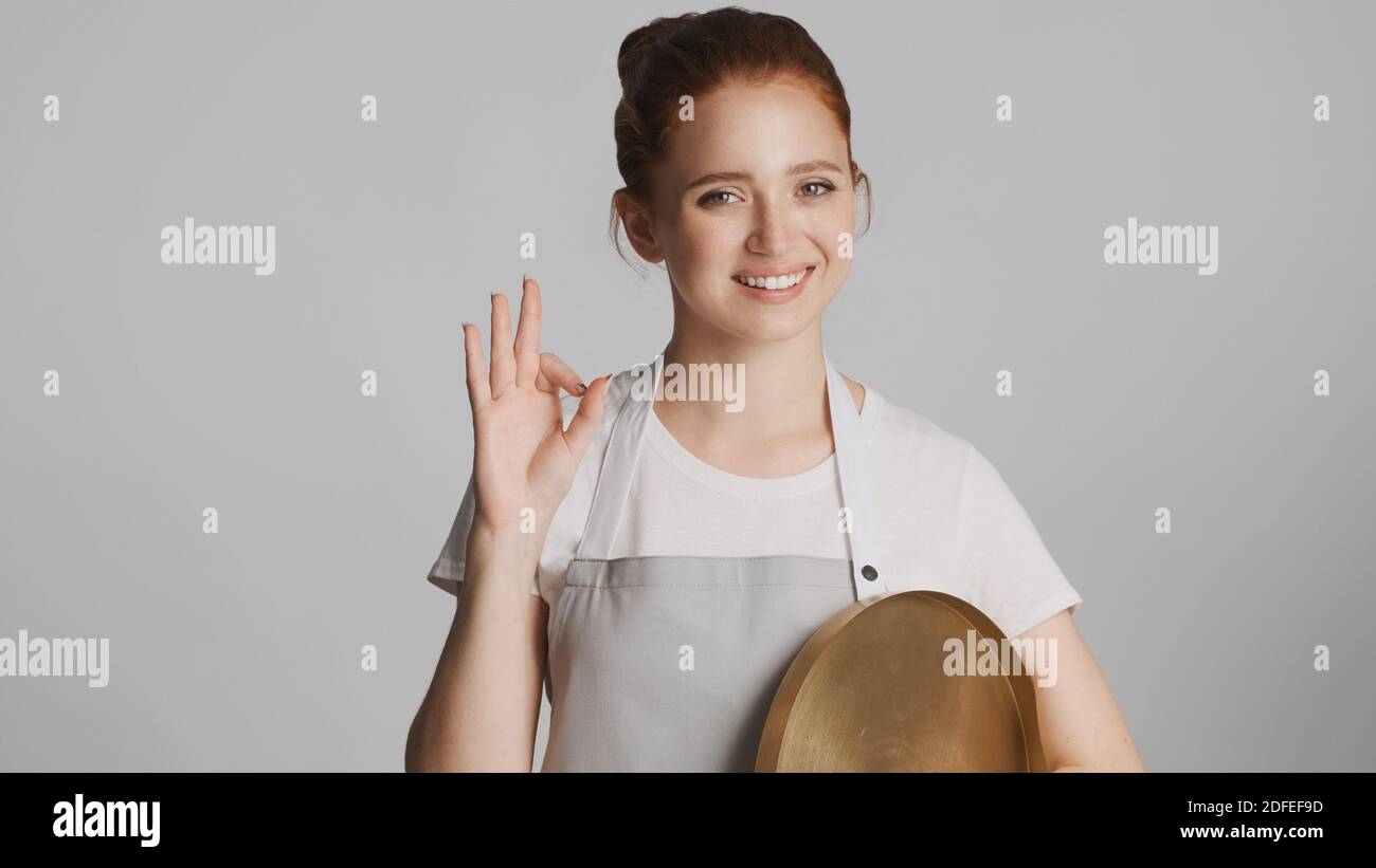Attractive waitress in apron with tray happily showing ok gesture on ...