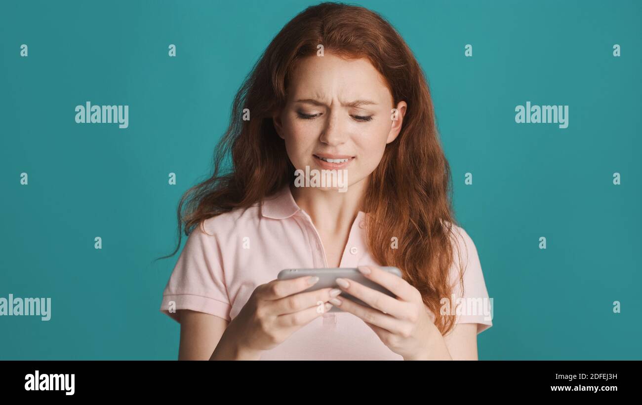 Attractive nervous girl playing in game on smartphone over colorful ...