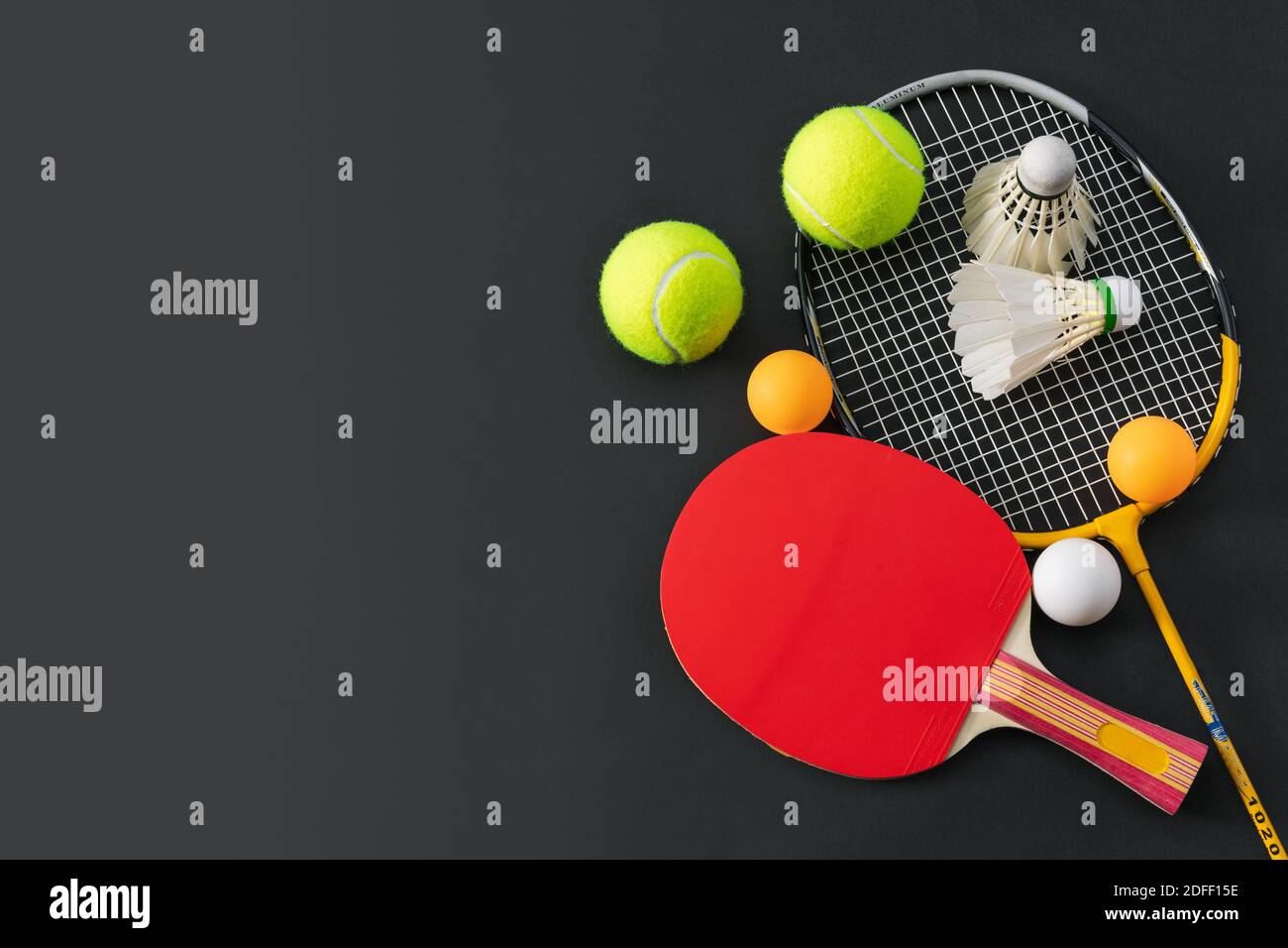 A high angle shot of ping pong balls and rackets on a black surface ...