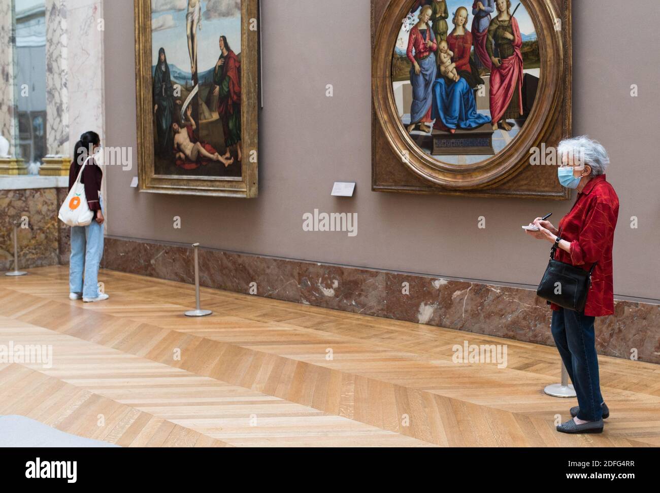 Tourists wearing protective face mask walk in the Denon Wing as they ...
