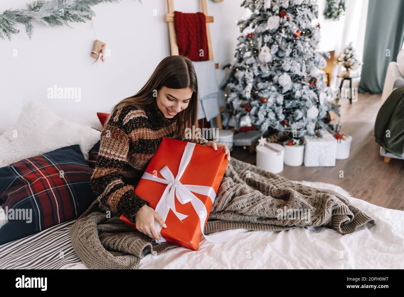 Happy caucasian woman holding big Christmas present while sitting on a ...