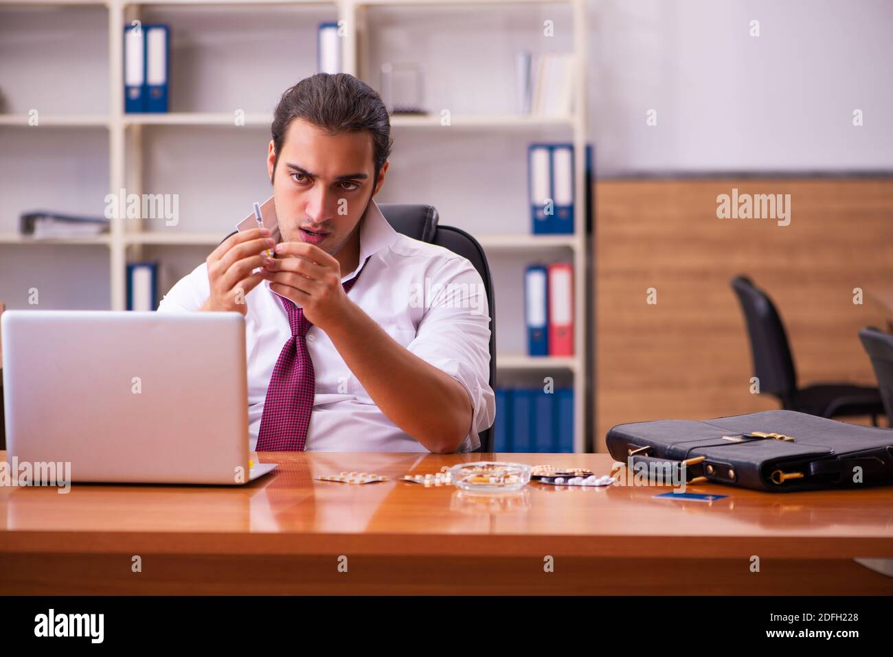 Young drug addicted male employee sitting at workplace Stock Photo - Alamy