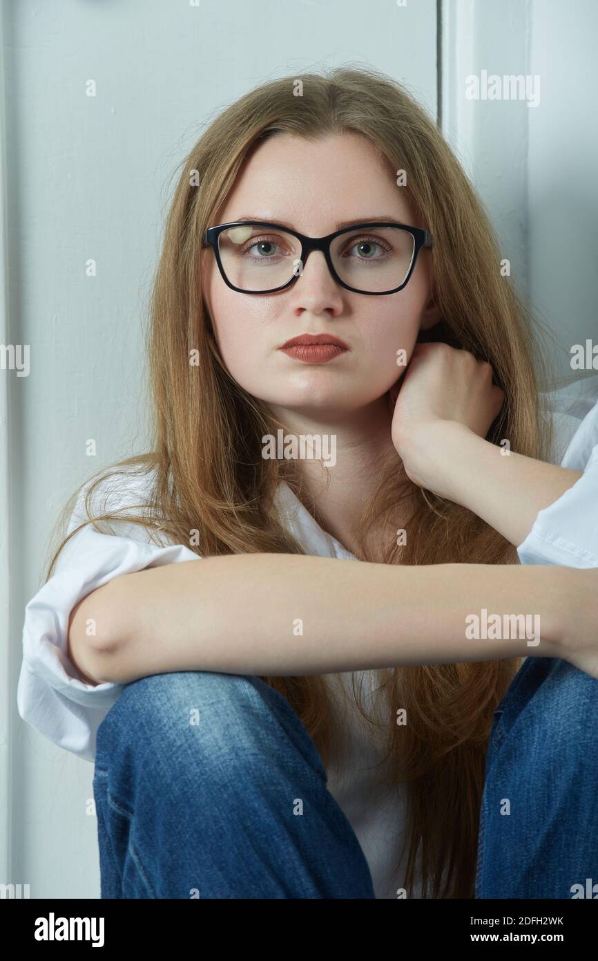 Sad Young Woman In Eyeglasses Sitting In Corner Looking At Camera Stock