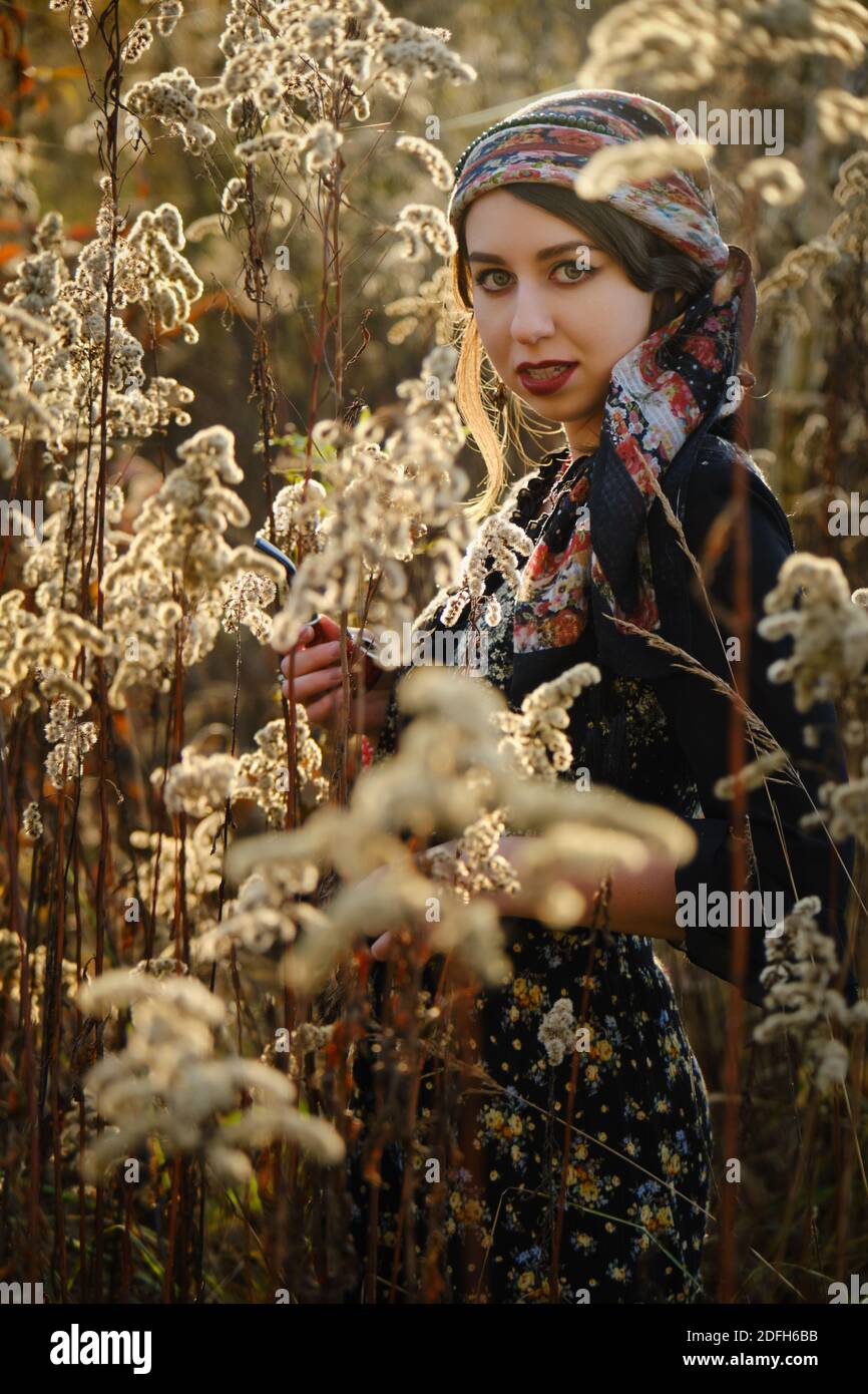 young gypsy woman smoking pipe in autumn dry grass, looking at camera ...