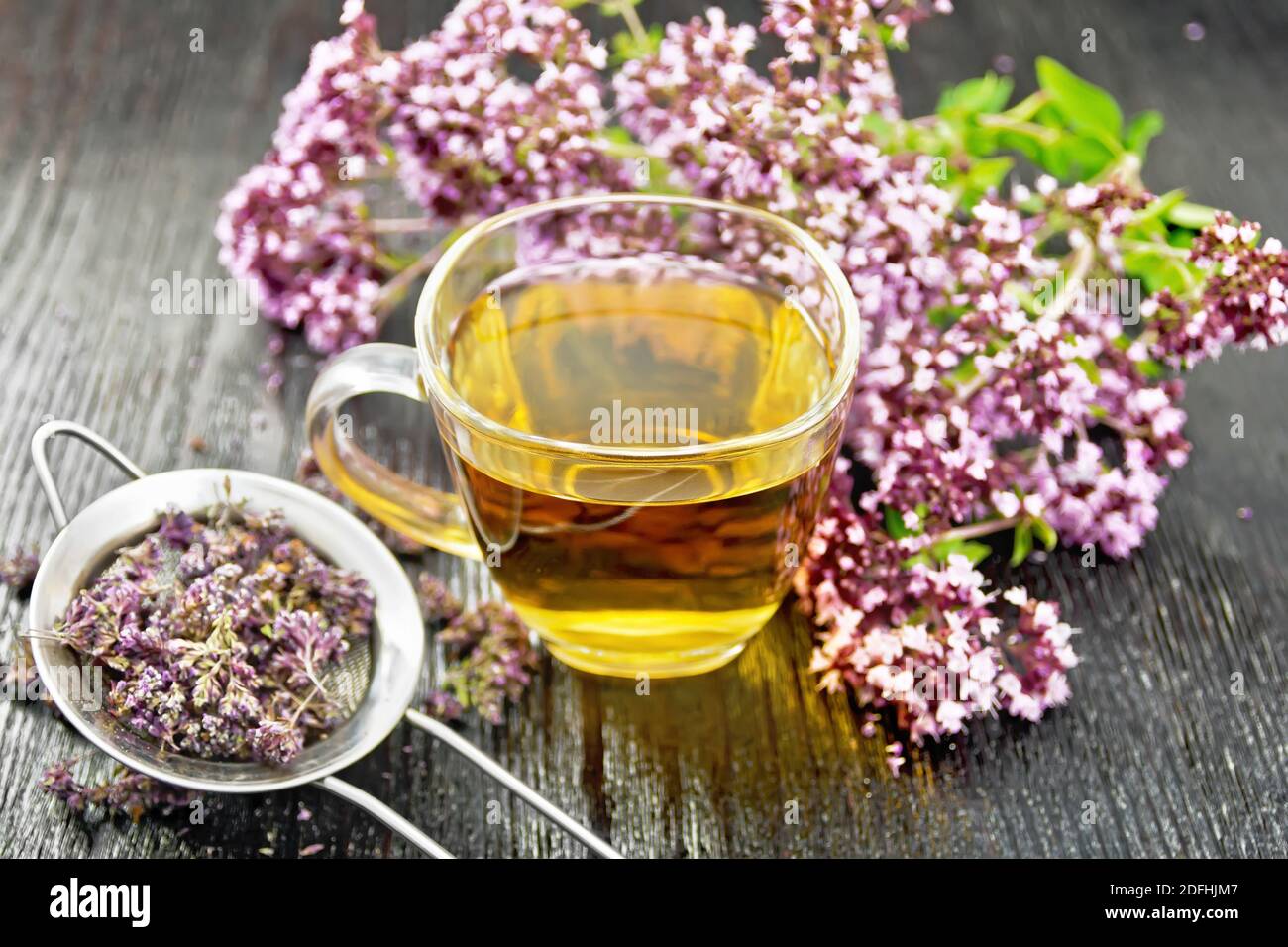 Oregano herbal tea in a glass cup, fresh marjoram flowers and a metal ...