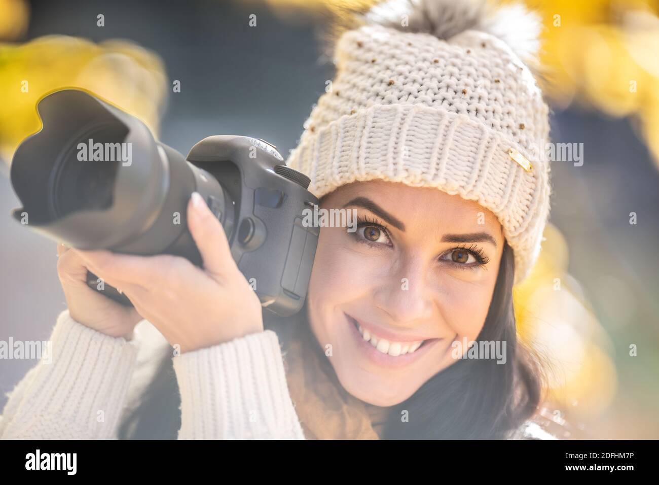 Smiling good-looking female photographer in a pompom hat takes pictures ...