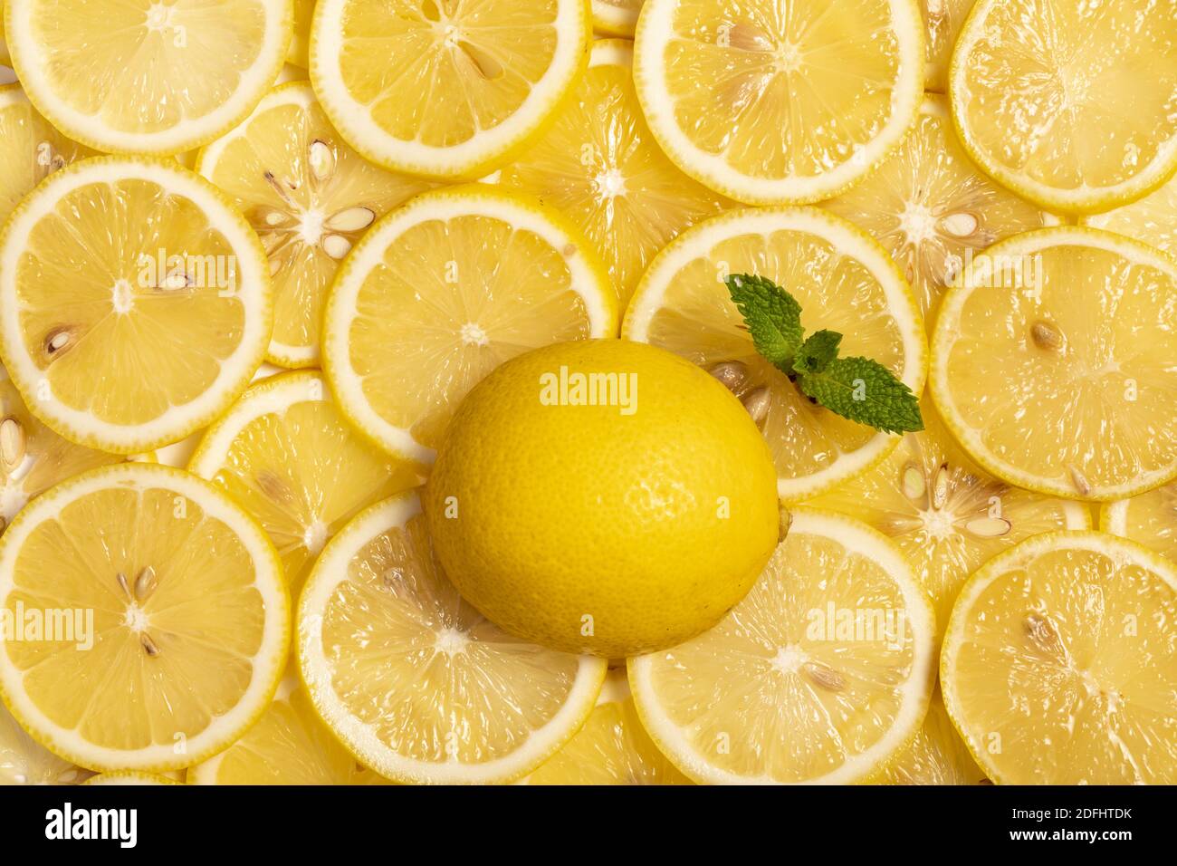 A top view of a whole lemon and mint leaves on a surface full of sliced ...