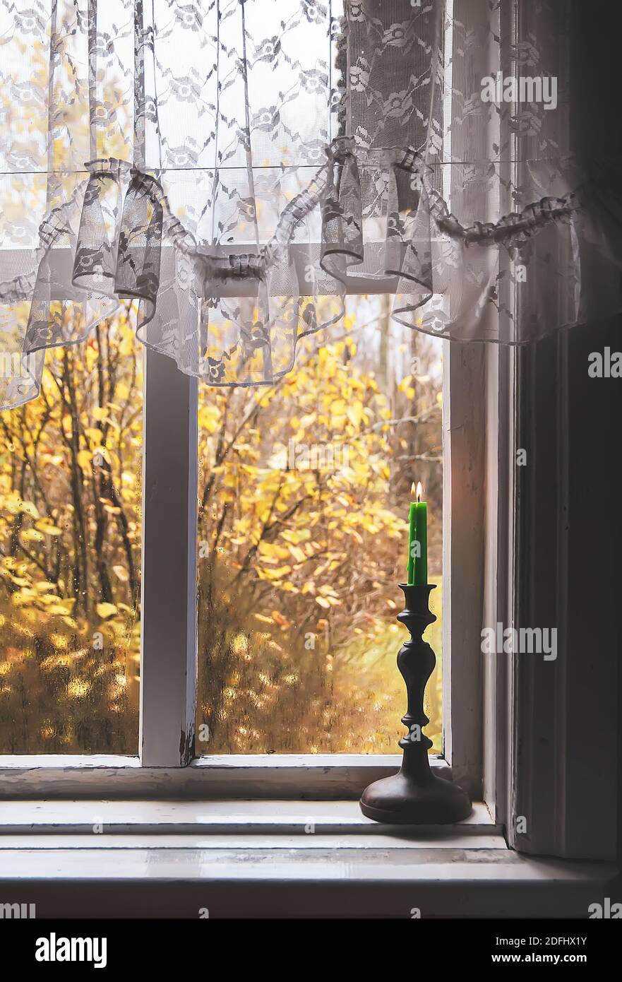 Burning wax candle in brass candlestick on the wooden window sill of in ...