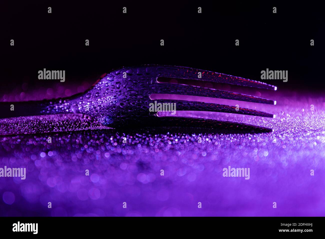 Single fork with waterdrops, in the dark illuminated with colourful ...