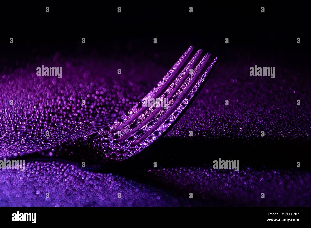 Single fork with waterdrops, in the dark illuminated with colourful ...