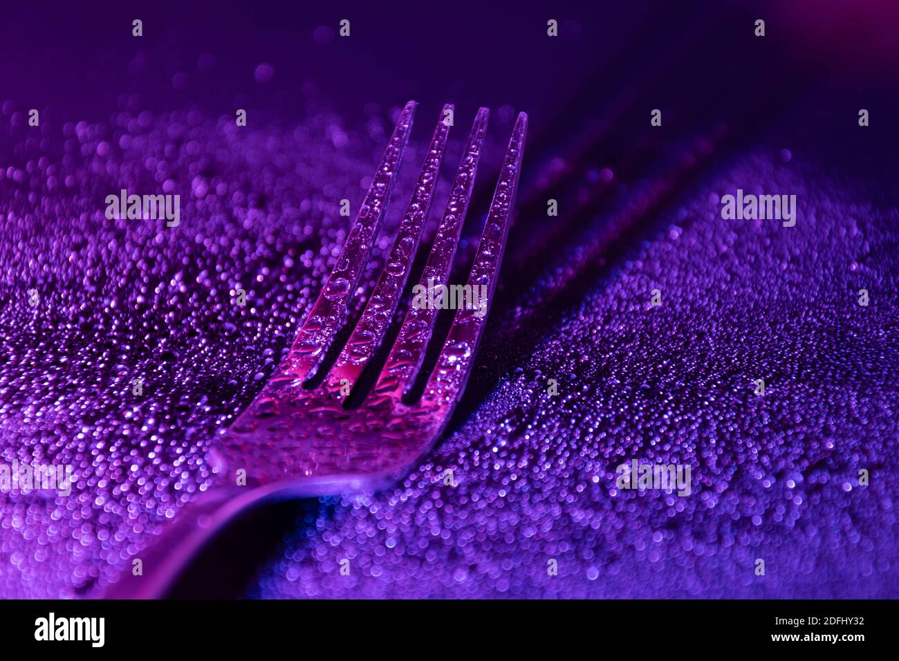Single fork with waterdrops, in the dark illuminated with colourful ...