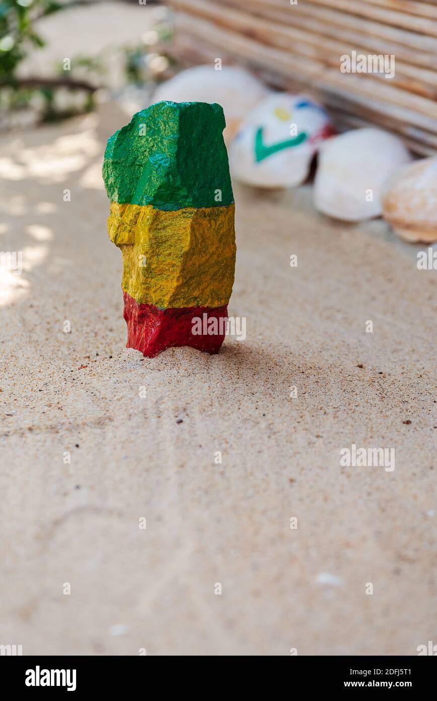 A stone on a sandy beach painted in Ghana's colors green, yellow and ...
