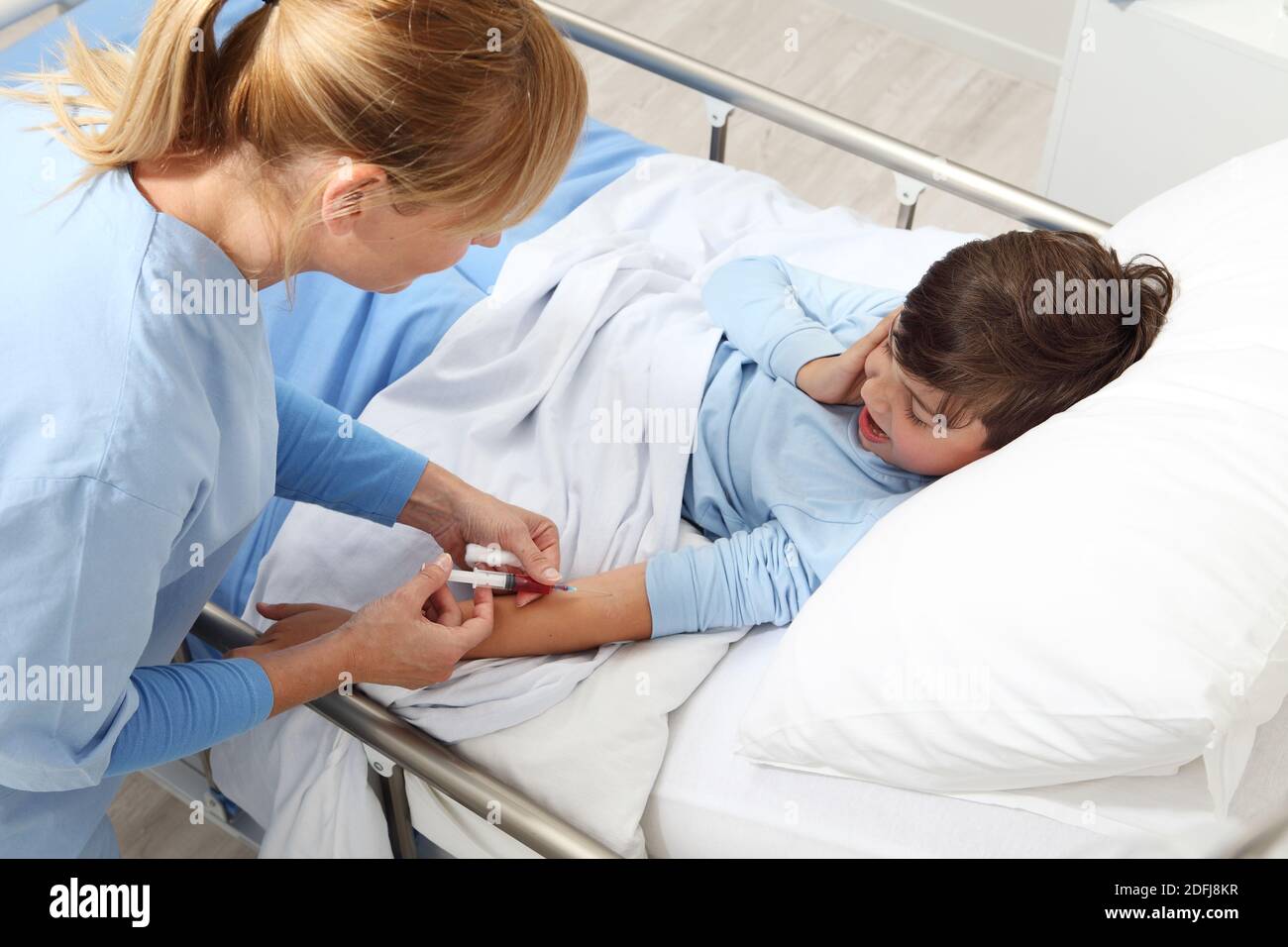 nurse makes a blood test to the sick child in bed in the hospital room ...