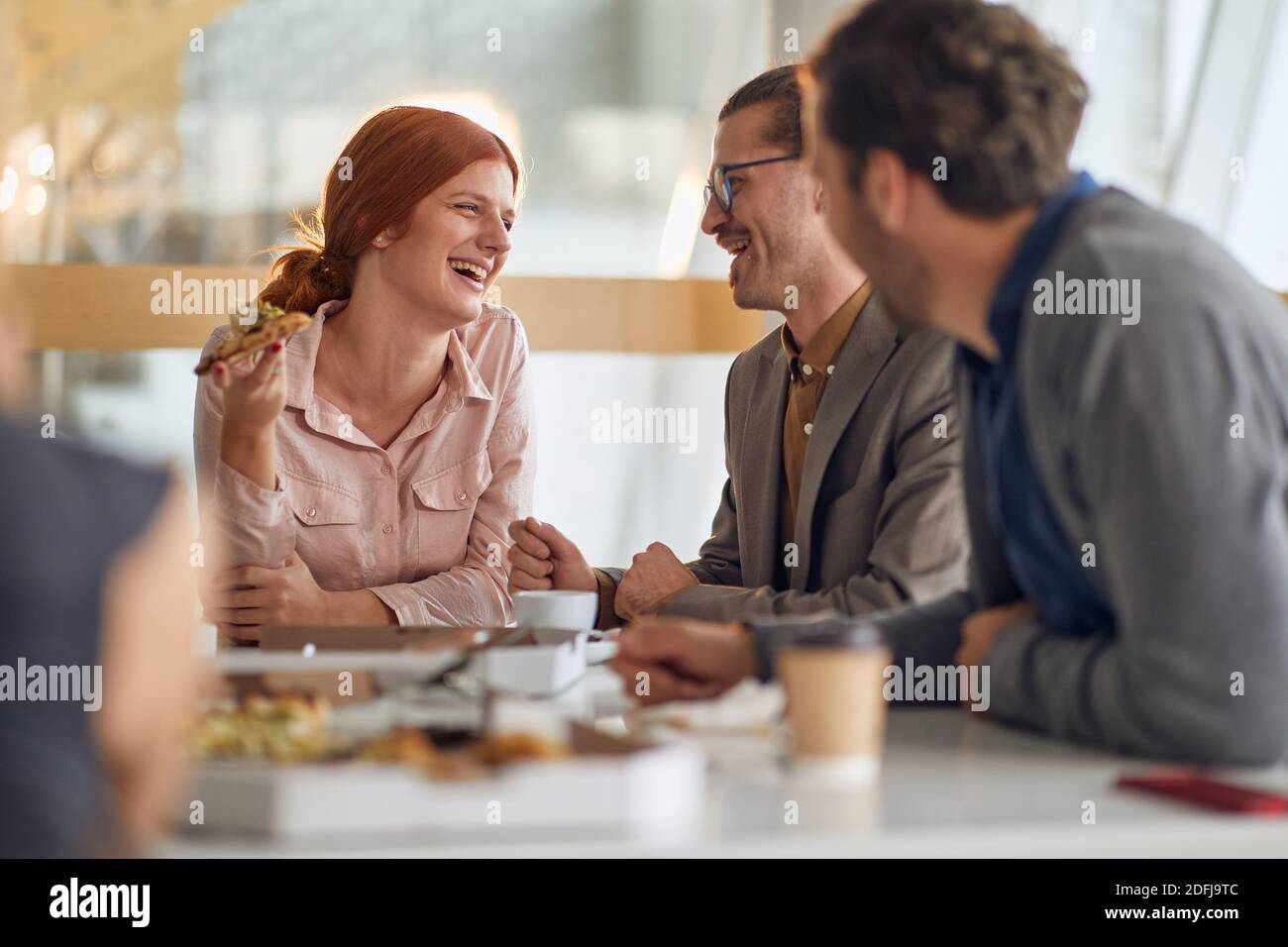 Employees eating pizza together at lunch break at company canteen in a ...