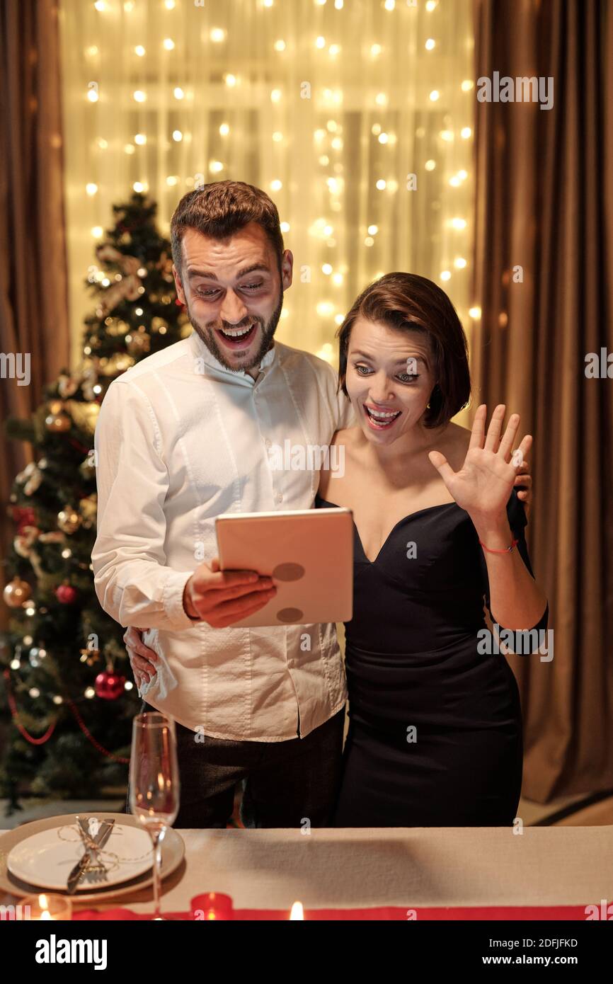 Young cheerful elegant couple looking at smartphone screen while ...